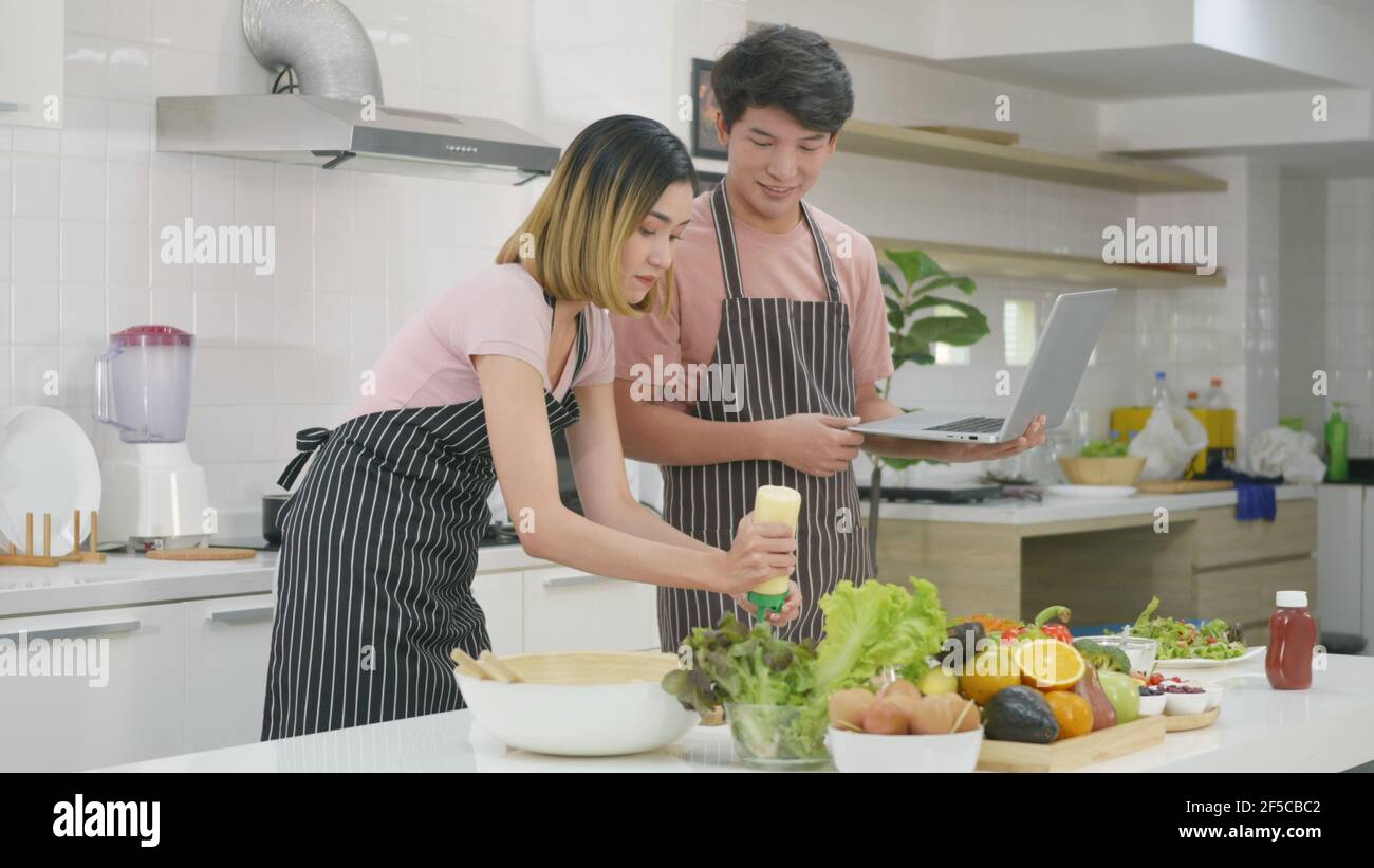 Happy Asian beautiful young family couple husband and wife cooking food vegetable salad in ...