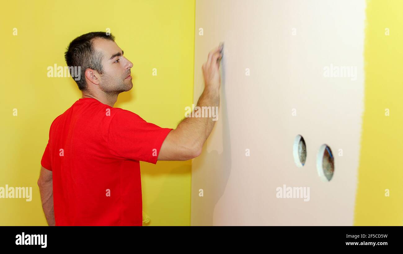 Portrait of room painter in action. A hand sanding the wall with a ...