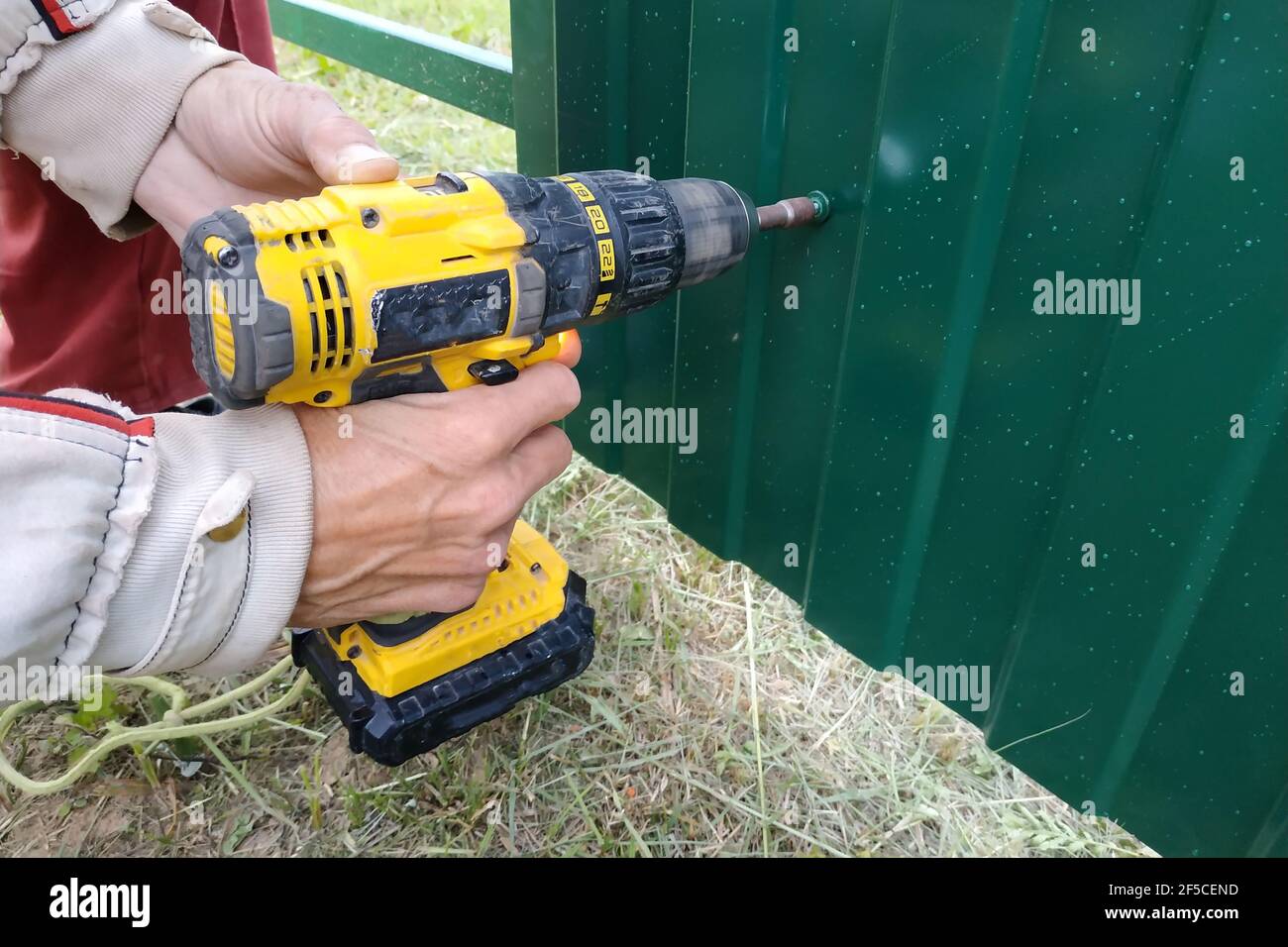The worker with a screwdriver screws the screws into the fence ...