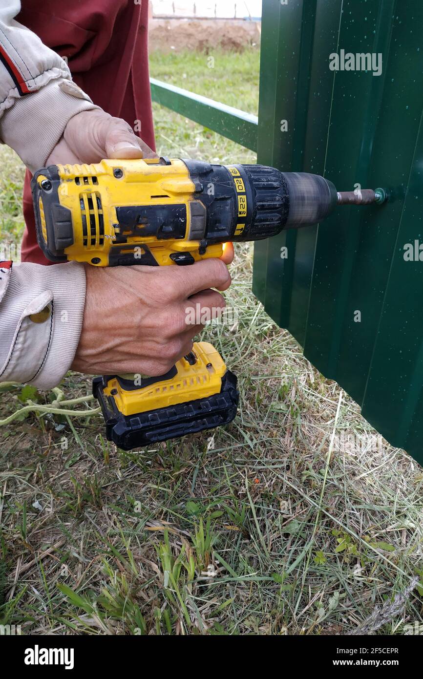 The worker with a screwdriver screws the screws into the fence ...