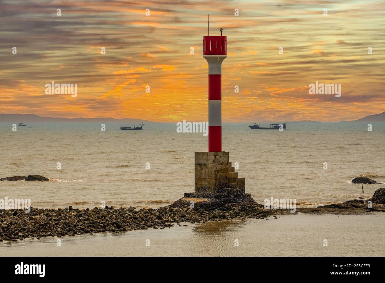 The beacon lighthouse under the gorgeous sunset by the sea Stock Photo ...