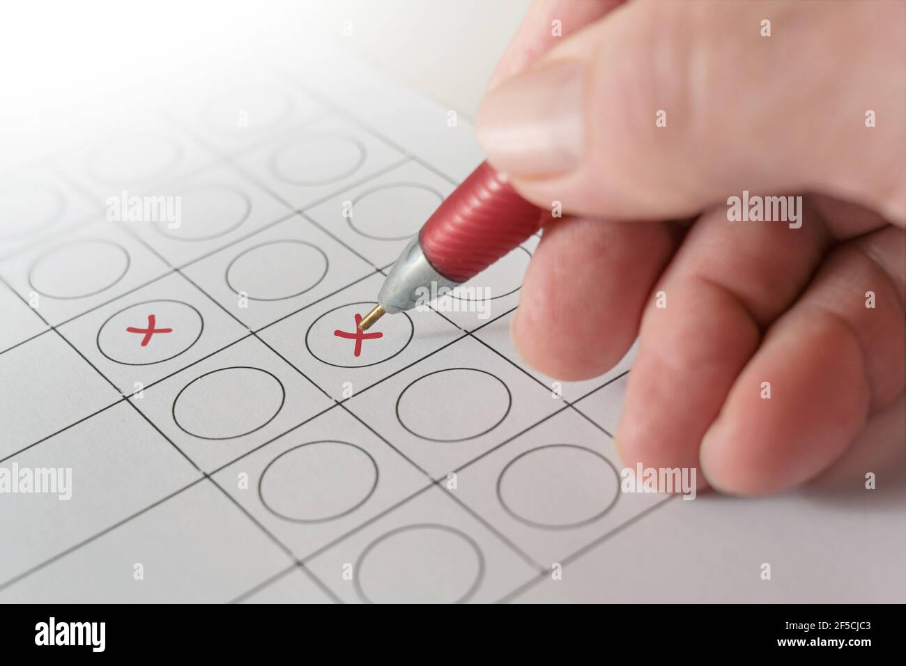 Hand holding a red ballpoint pen and makes crosses on a ballot paper ...