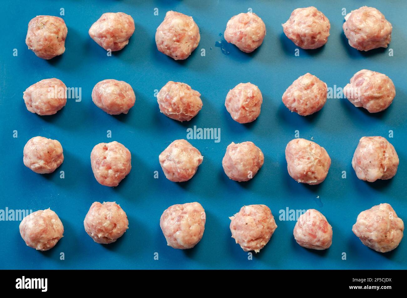 Raw shaped meatballs in sunbeams on blue. Rows of meatballs with pepper ...