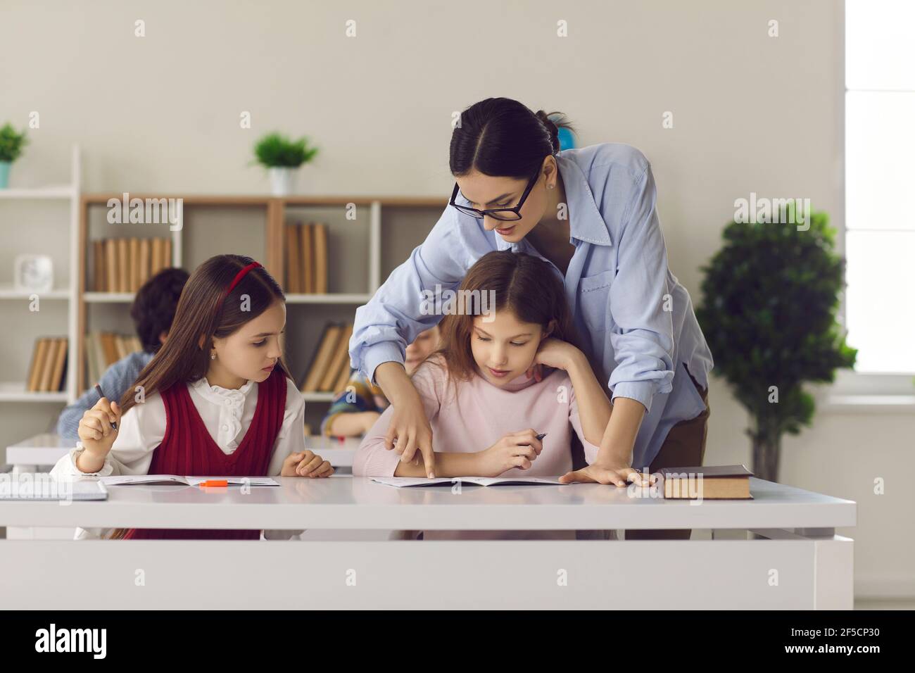 Young elementary school teacher helping her students who are writing in ...