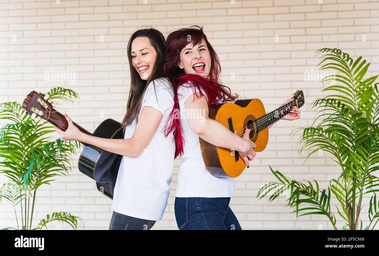Side view of young women smiling and playing Spanish guitars while ...