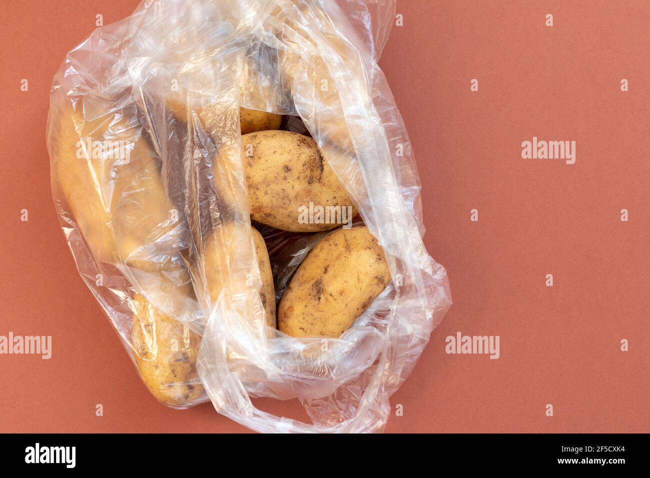 fresh young potatoes in a plastic bag on brown background, zero waste ...