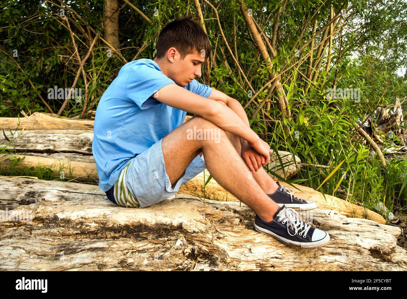 Sad Young Man sit on the Log outdoor Stock Photo - Alamy