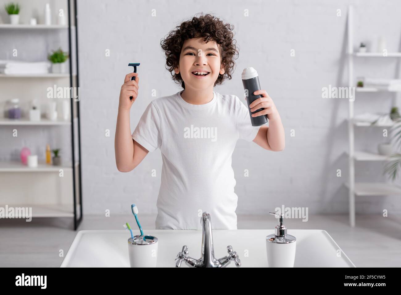 Smiling arabian boy holding razor and shaving foam in bathroom Stock ...