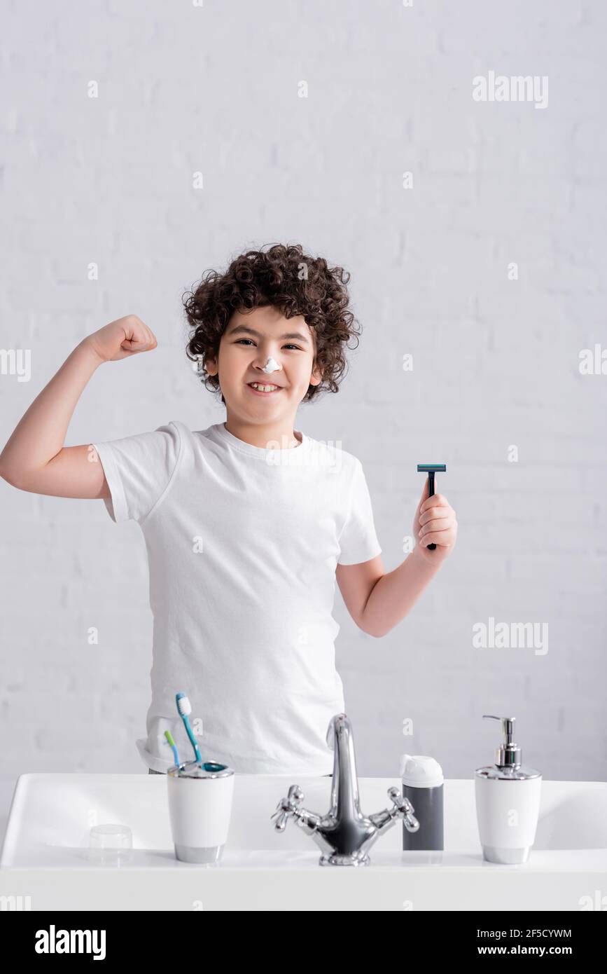 Smiling arabian boy with shaving foam on nose holding razor and showing ...