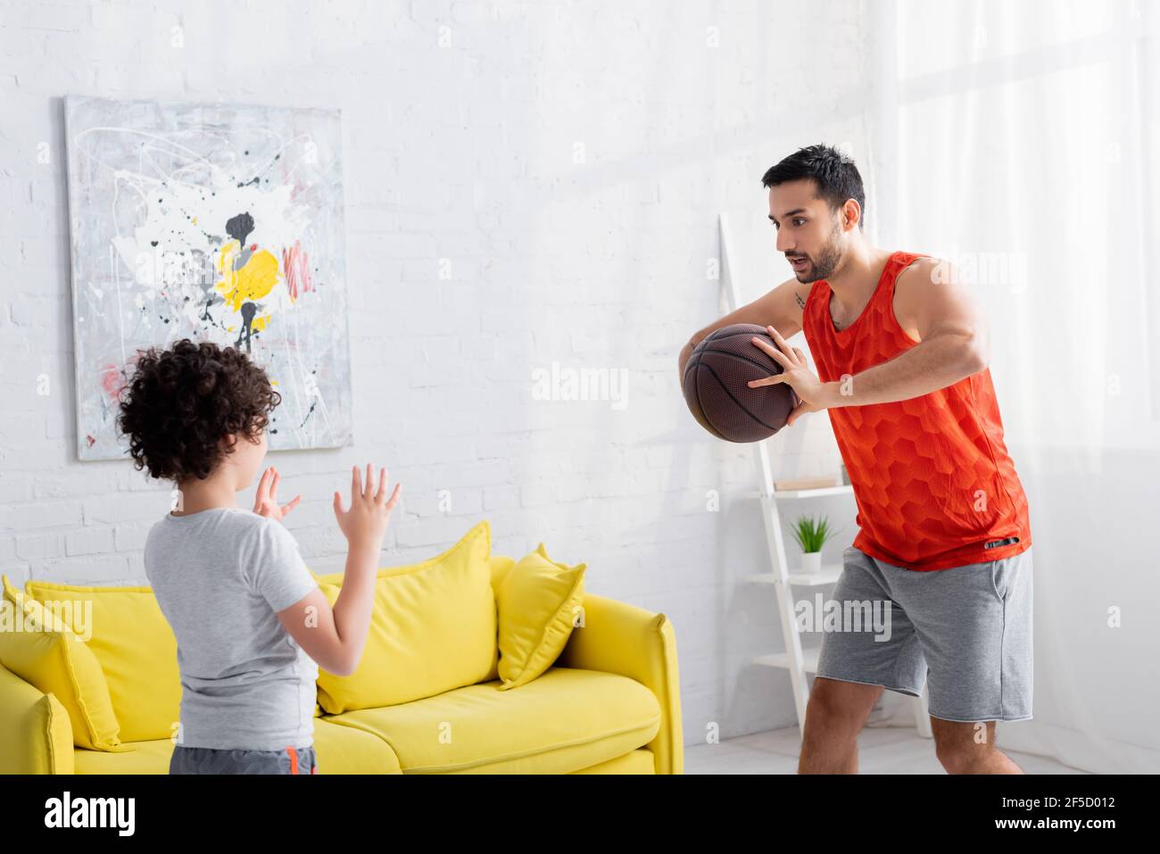Muslim man playing basketball with son in living room Stock Photo - Alamy