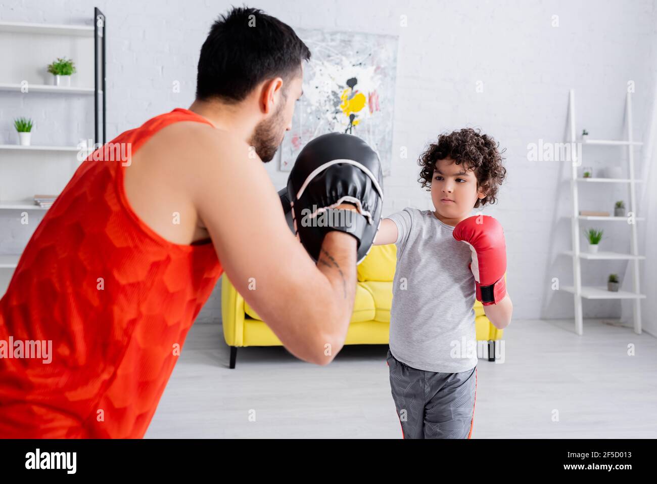Arabian boy boxing with father on blurred foreground in living room ...