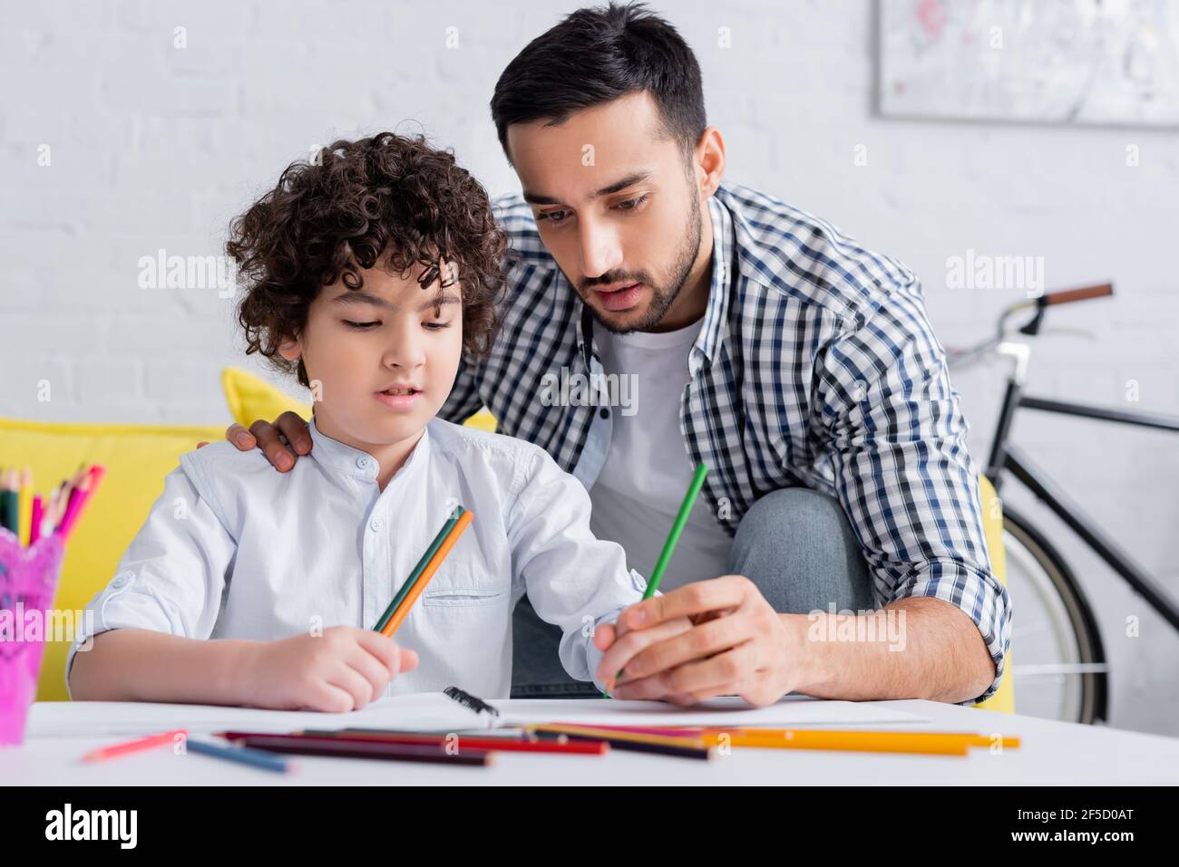 young muslim man helping son drawing with pencil on blurred foreground ...