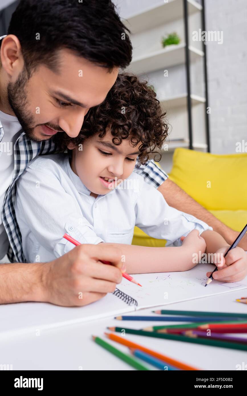 happy arabian dad and son drawing with pencils in sketchbook together ...