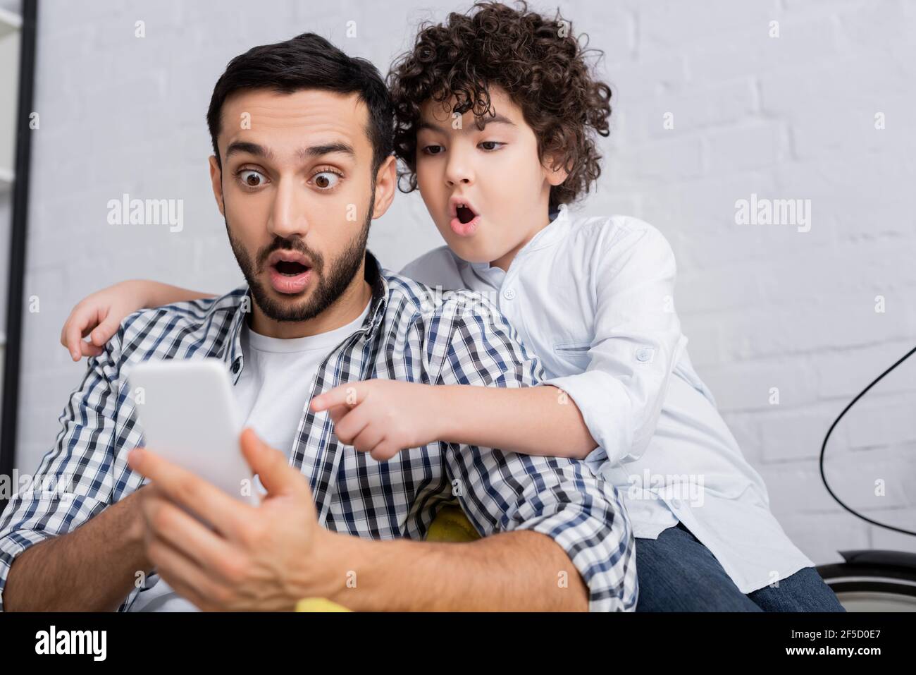astonished muslim boy pointing at smartphone near shocked father on ...