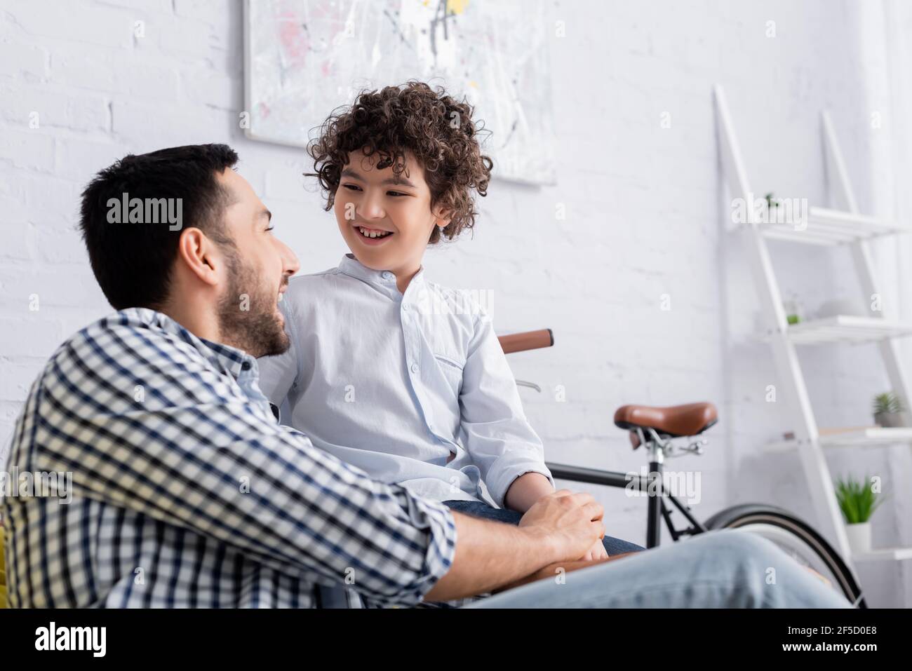 happy muslim father and son looking at each other while talking at home ...
