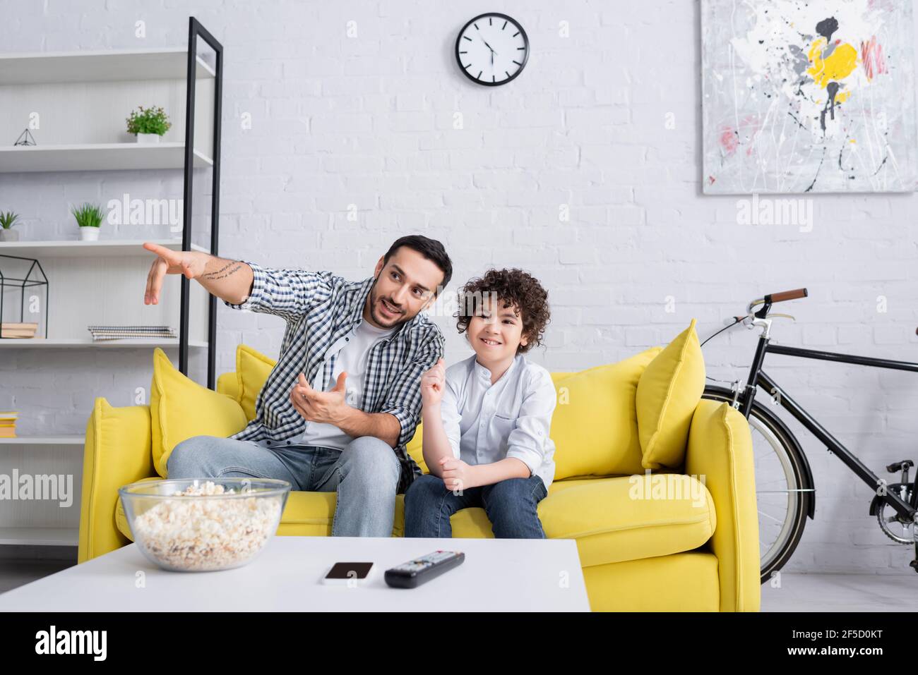 smiling arabian man pointing with fingers while watching tv with son at ...