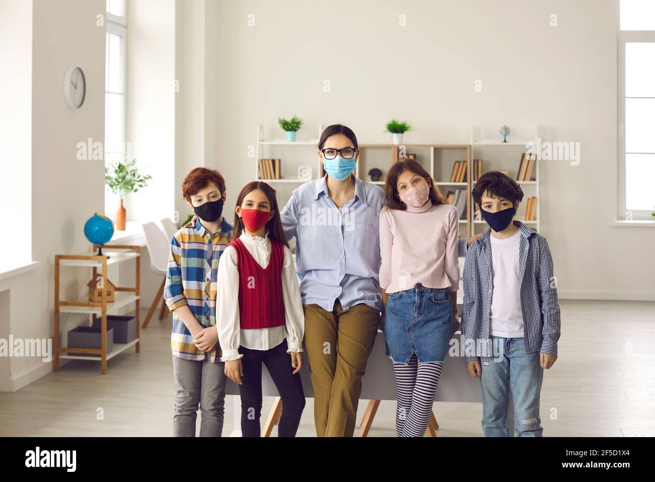 Teacher and pupils group wearing medical face mask looking at camera ...