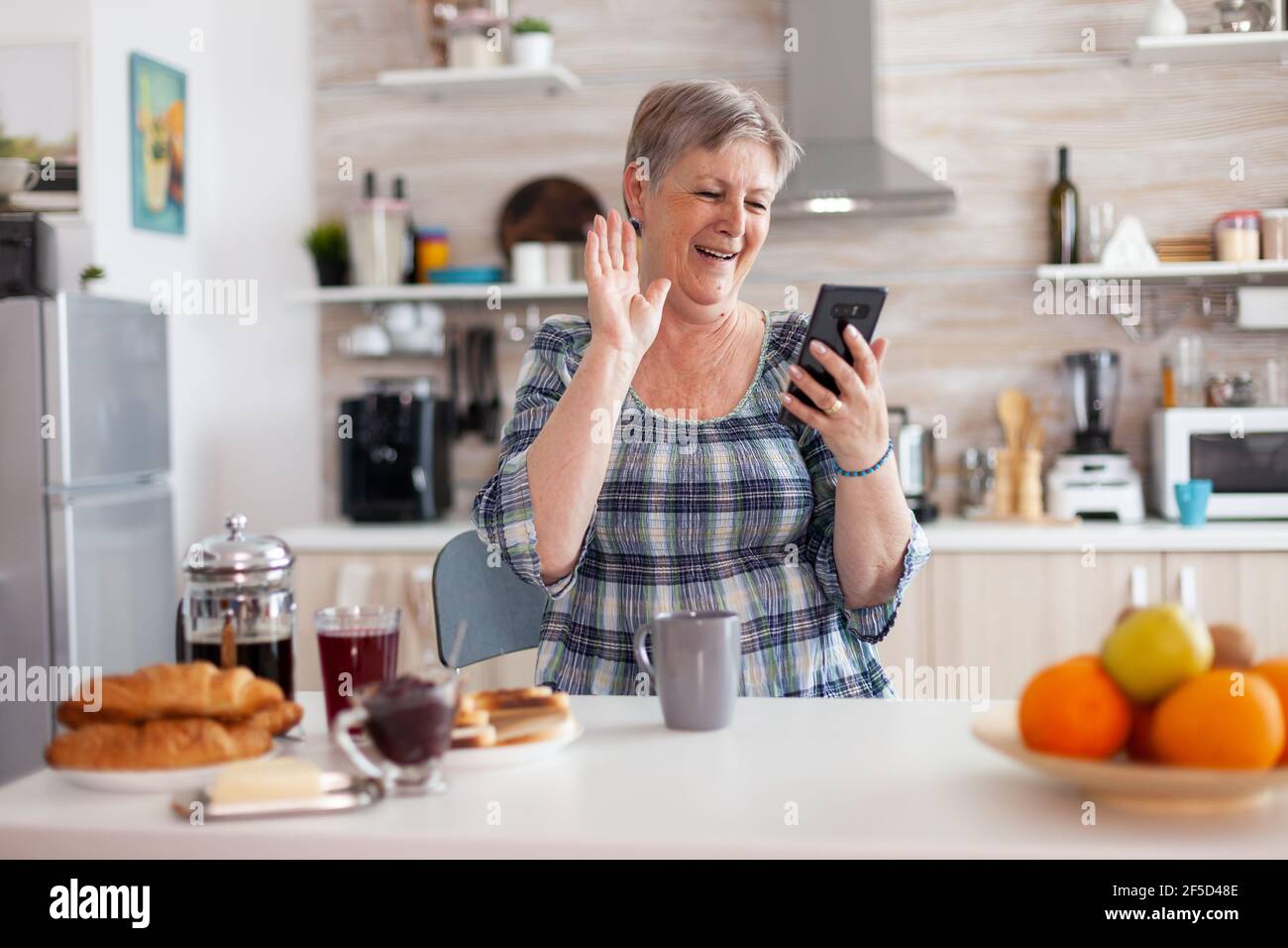 Senior woman saying hello while having video call with family using ...