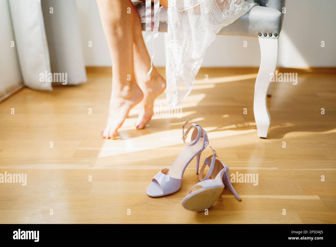 Barefoot bride sits in a chair in a hotel room during wedding ...