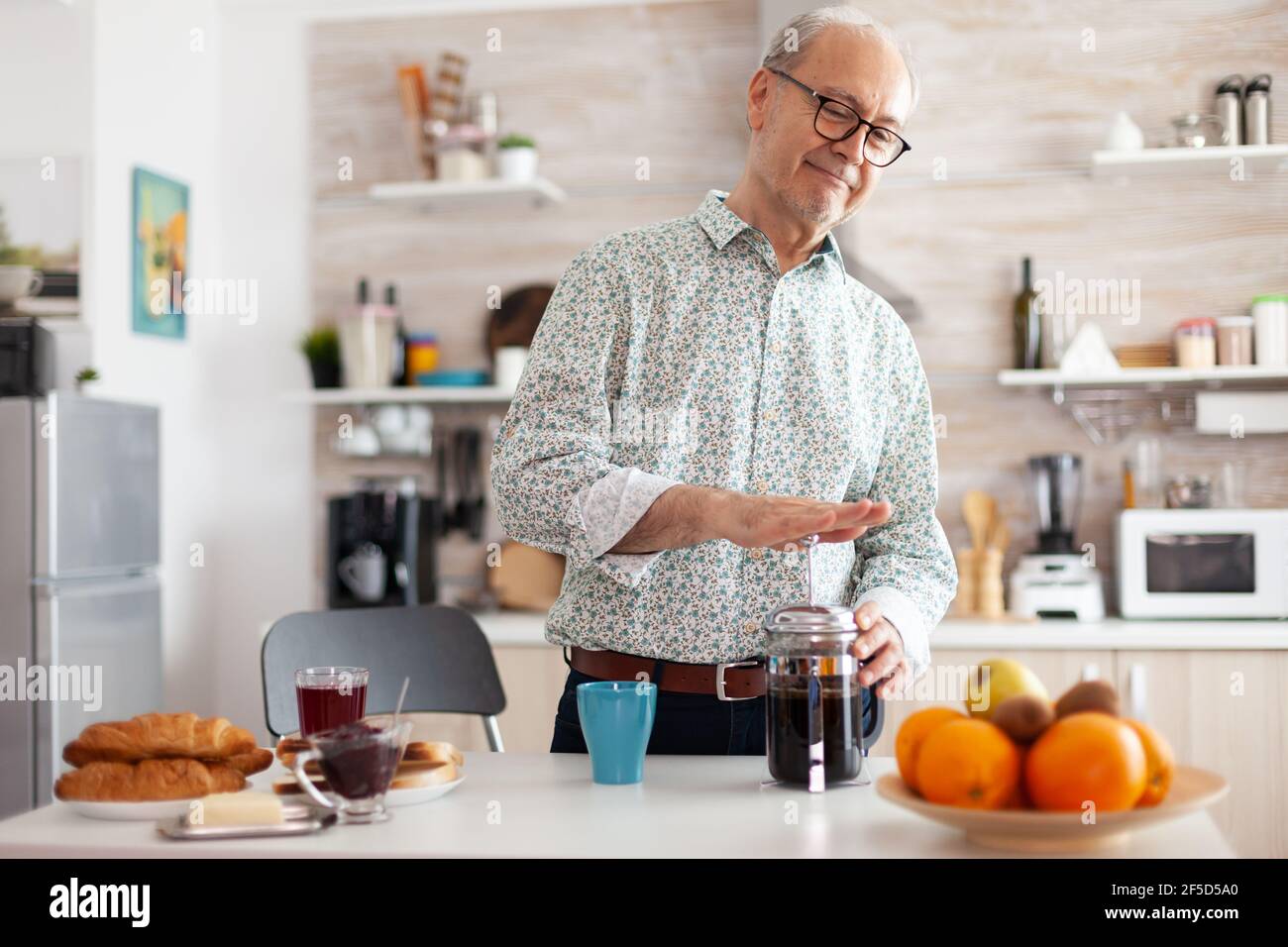 Senior man making coffee using french press during breakfast in kitchen ...