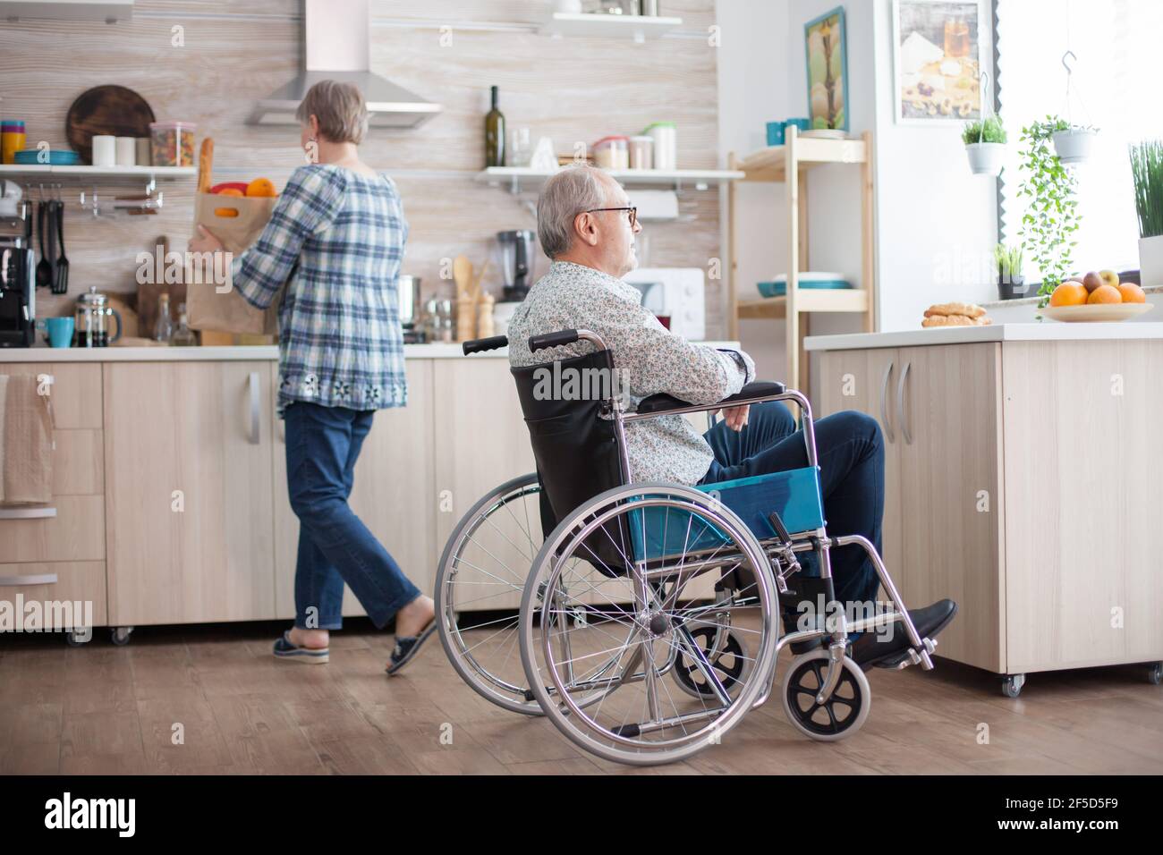 Invalid senior man smiling looking through the window in kitchen and ...