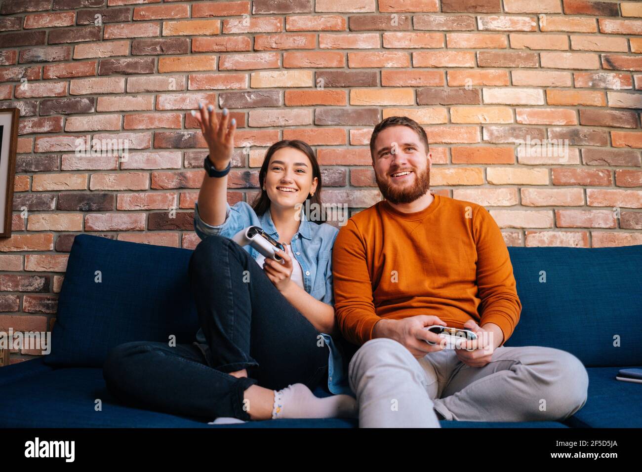 Portrait of happy cheerful young couple holding controllers and playing ...