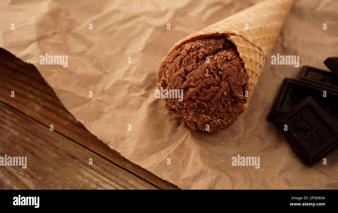 Chocolate ice cream in a waffle cone on craft paper on a wooden ...
