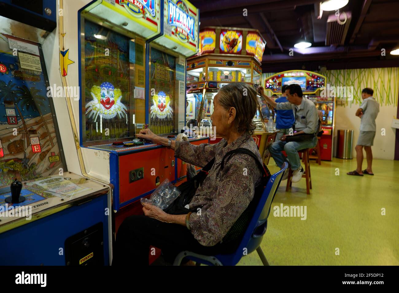 Old grandma woman sitting and playing games at a local arcade in Wo Che ...