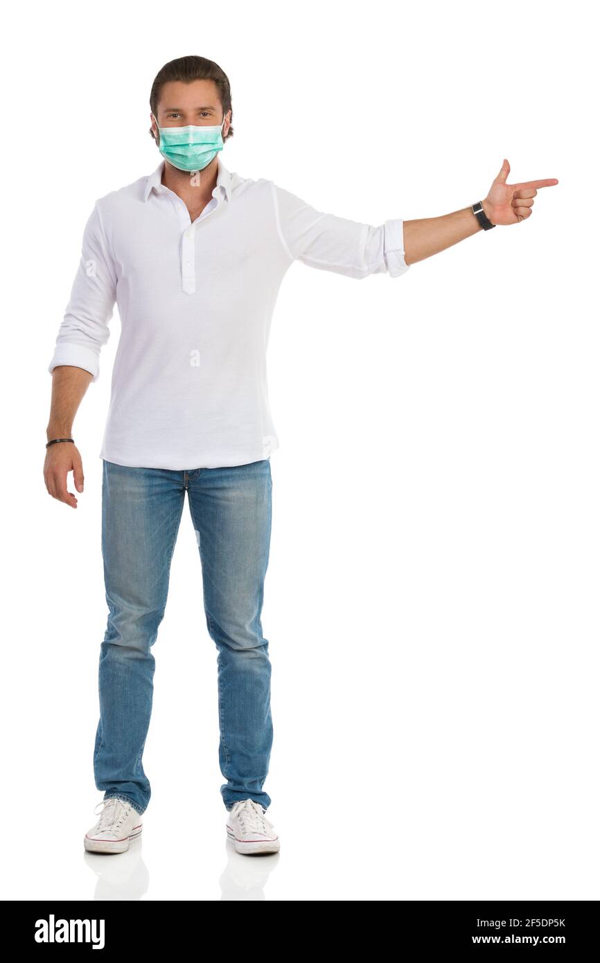 Handsome young man in protective face mask is standing and pointing at ...