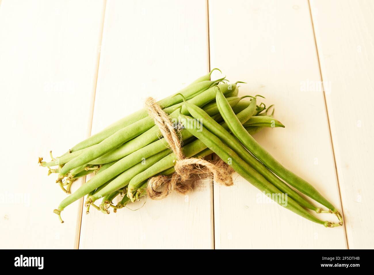 bunch of raw common green beans tied up with a string on white wooden ...