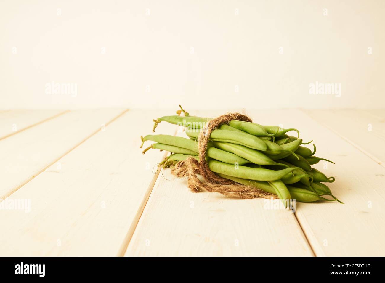bunch of raw common green beans tied up with a string on white wooden ...