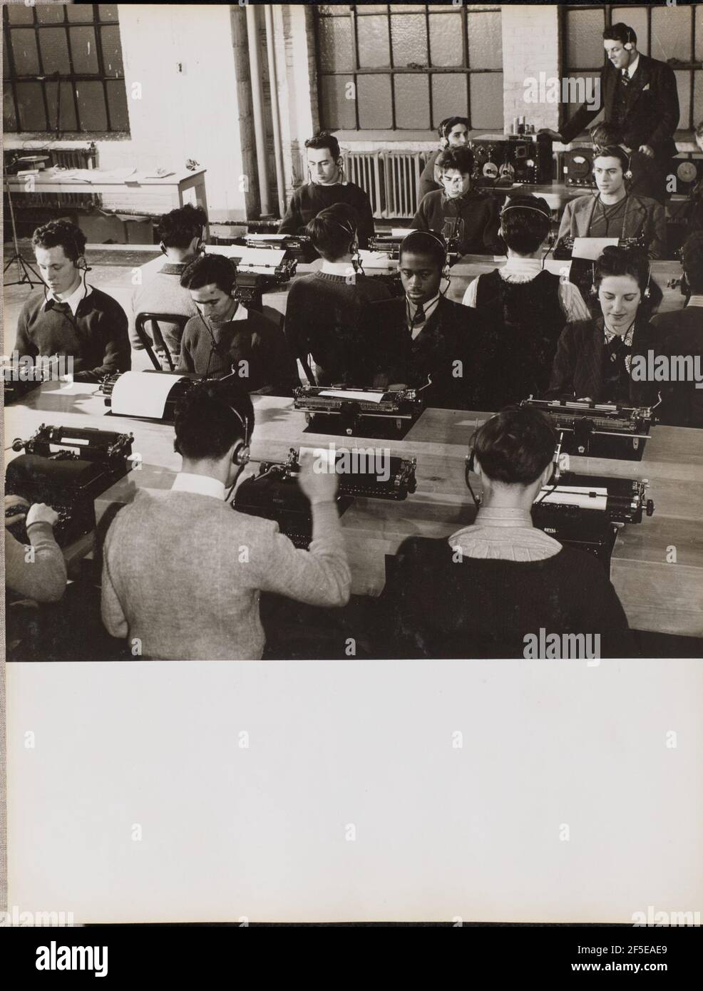 People sit in front of typewriters while wearing headphones. Arnold ...