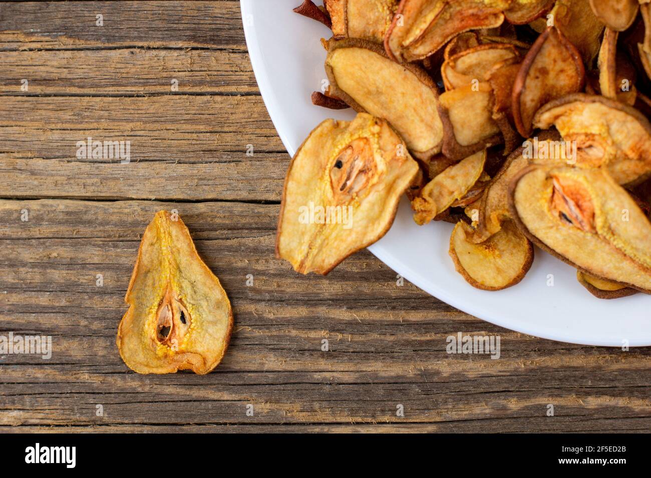 A pile of dried pears in slices on a white plate on wooden background ...