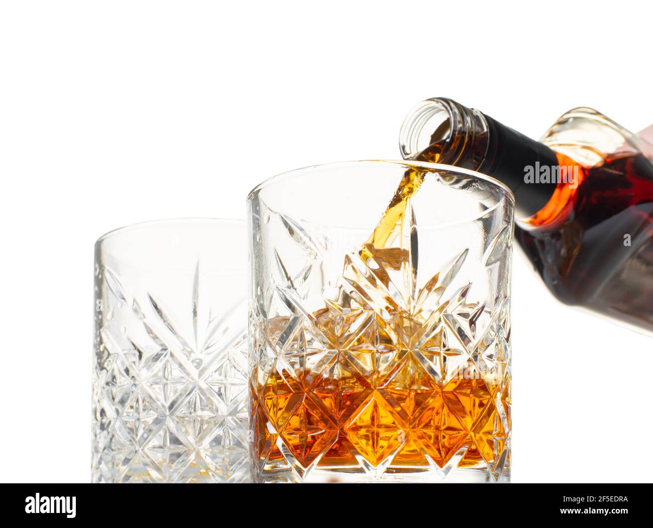 whiskey is poured into a glass from bottle on white isolated background ...