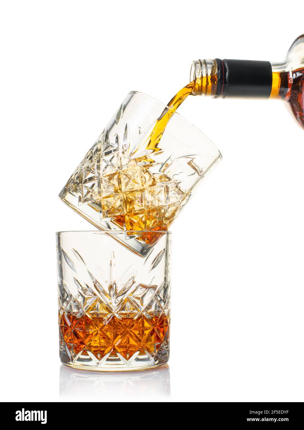 whiskey is poured into a glass from bottle on white isolated background ...
