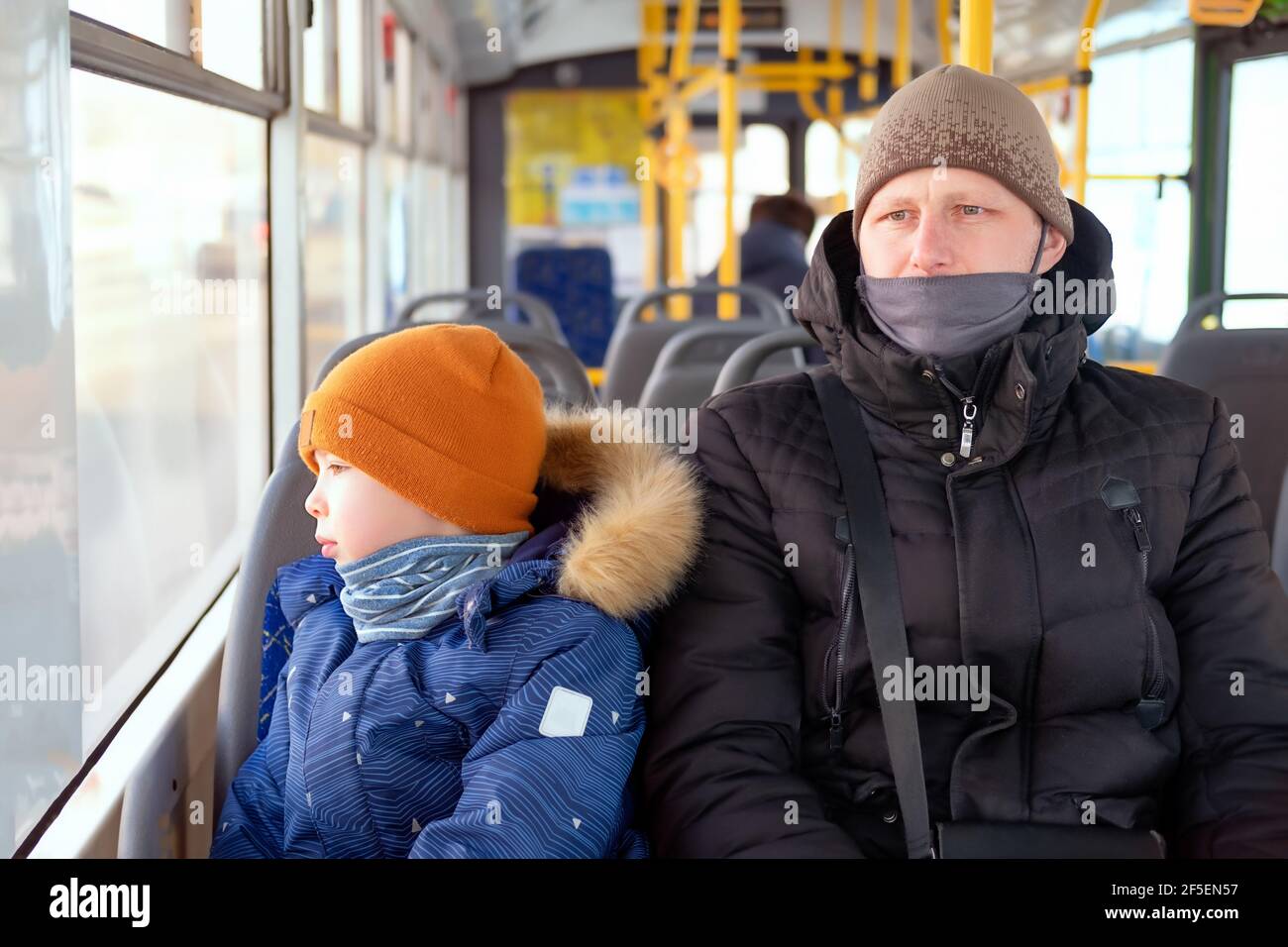 a man and a boy in a bus wearing medical masks. Dad and son in a public ...