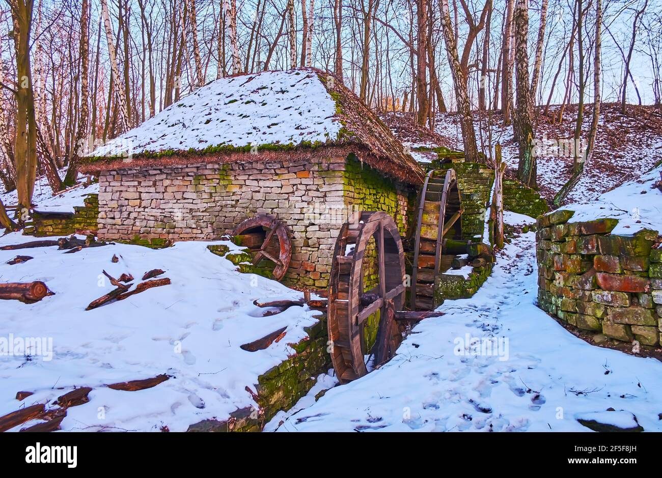 The old stone water mill at the foot of the snowy hill, surrounded with ...