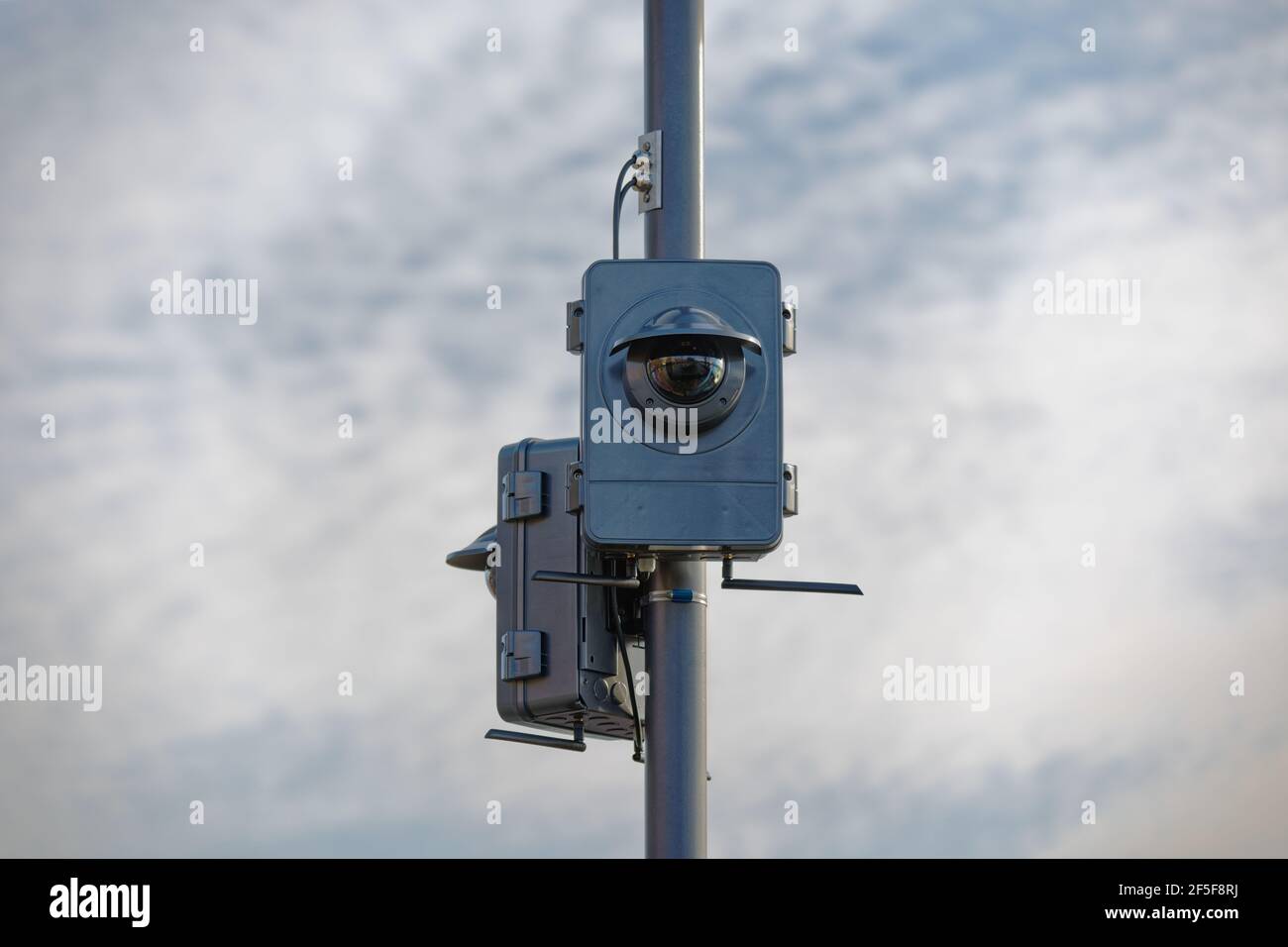 two large surveillance cameras on a light pole in cloudy sky with ...