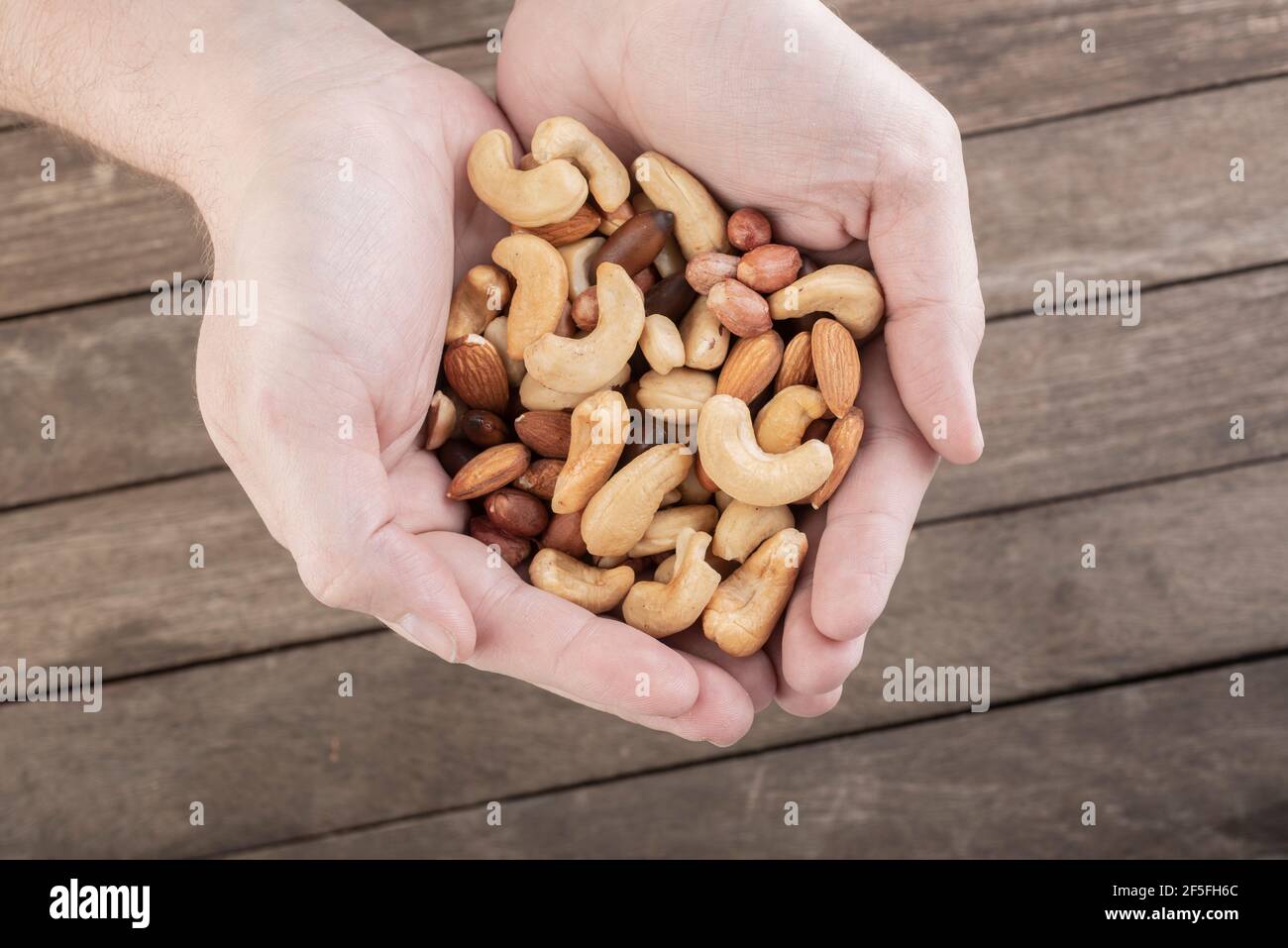 Hands full of mixed nuts over a wooden background. Peanuts, brazilian ...