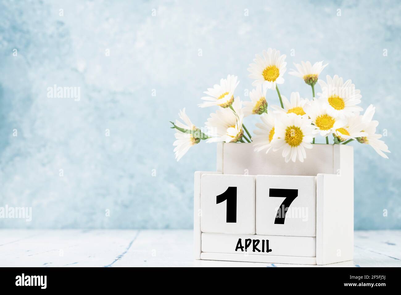 White cube calendar for april decorated with daisy flowers over blue ...