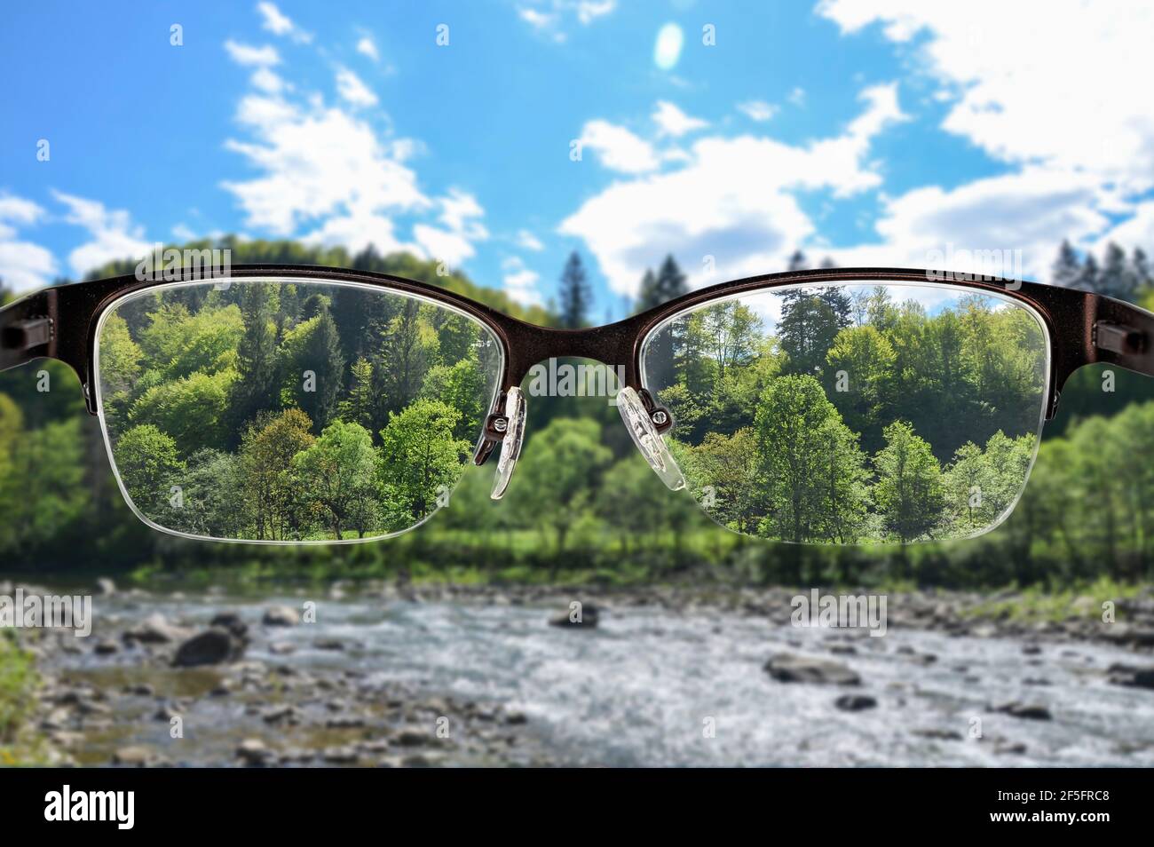 River and green forest landscape focused in women's glasses frame. View ...