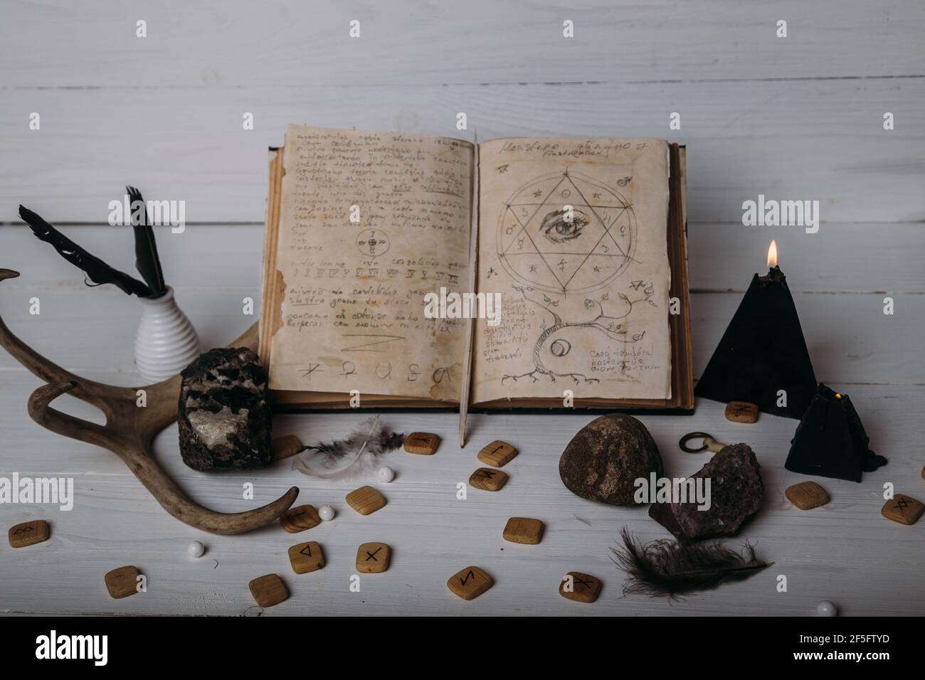 Open old book with magic spells, runes, black candle and herbs on witch ...