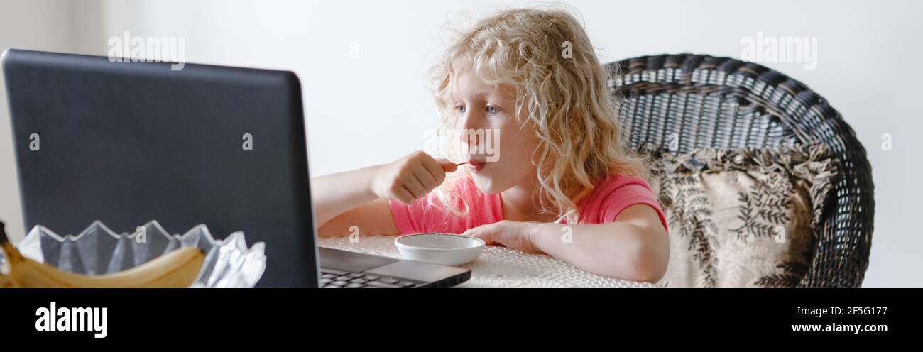 Young girl eating food and watching cartoons on laptop. Child with ...