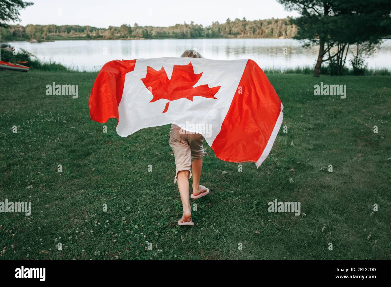 Girl wrapped in large Canadian flag by Muskoka lake in nature. Canada ...