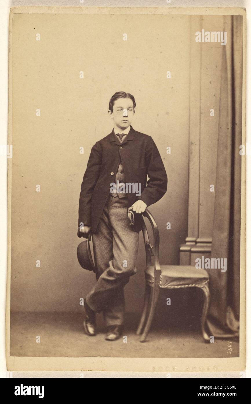 Unidentified young man with derby in hand, with other hand on chair ...