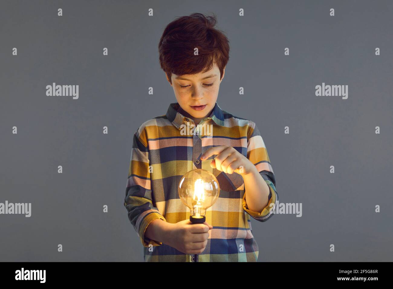 Boy touching glowing lightbulb lamp in hand stand isolated on studio ...