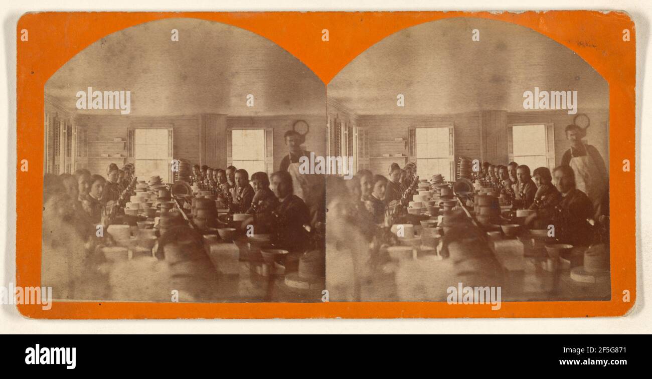 Interior of a hat factory: people around table full of hats. Z.B ...