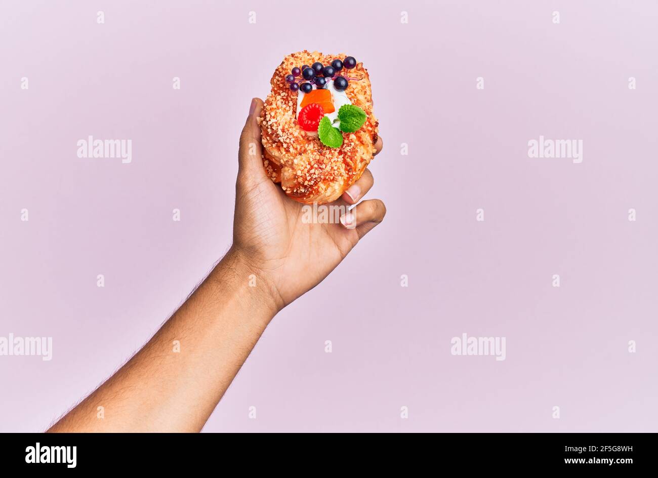 Hand of hispanic man holding sweet bun over isolated pink background ...
