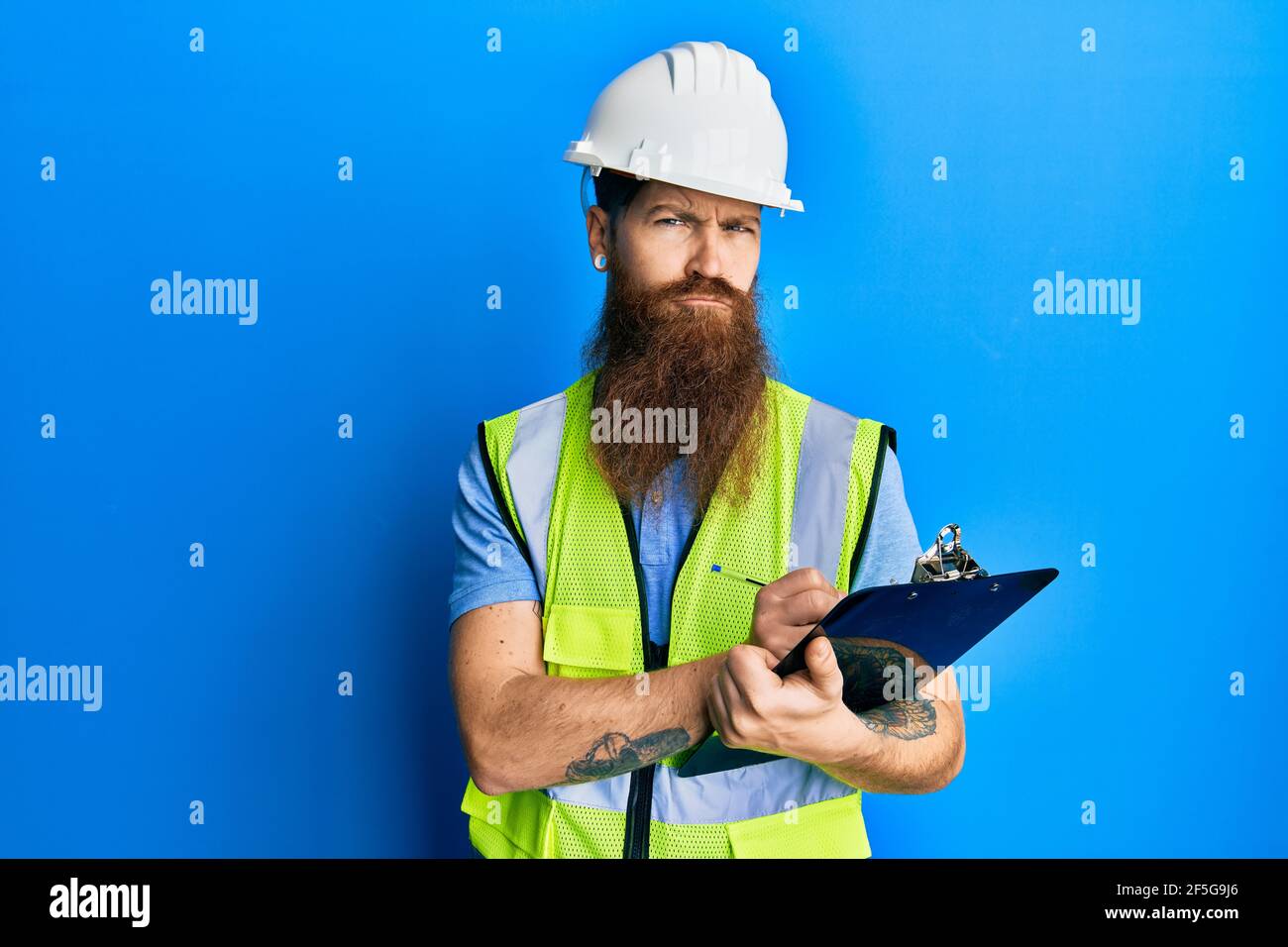 Redhead man with long beard wearing safety helmet holding clipboard ...