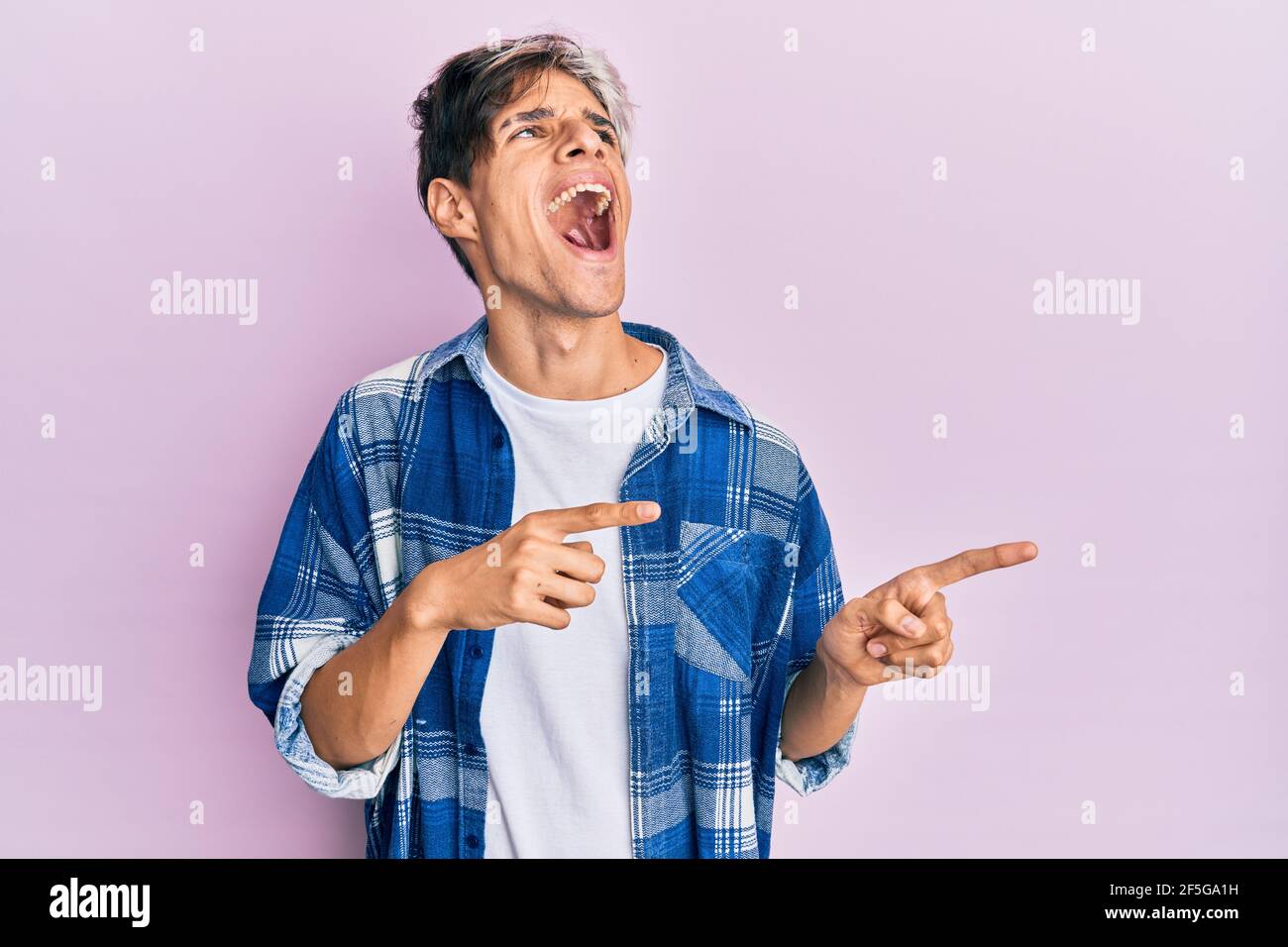 Young hispanic man pointing with fingers to the side angry and mad ...